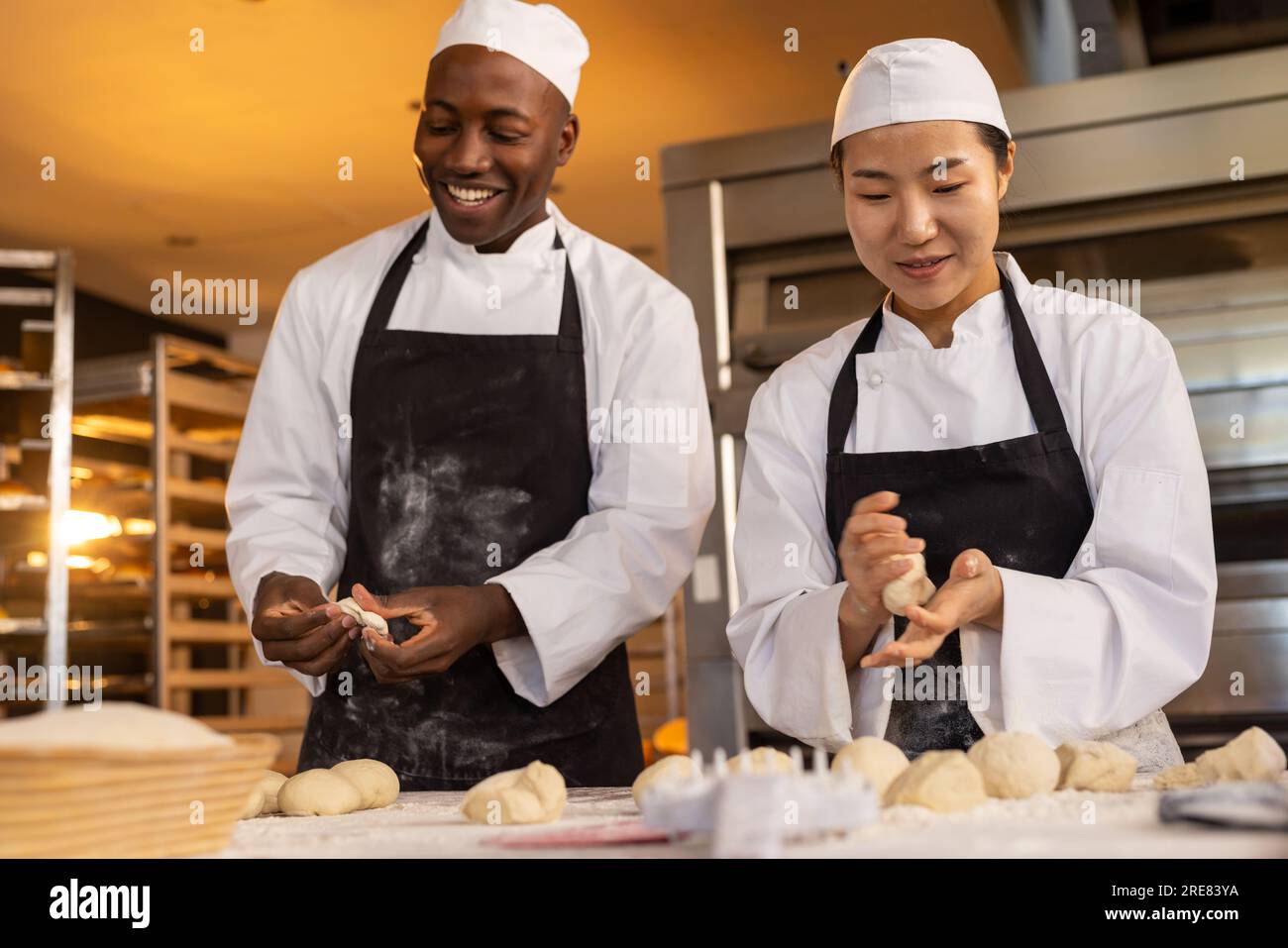 Happy diverse bakers wearing aprons in bakery kitchen and making rolls ...
