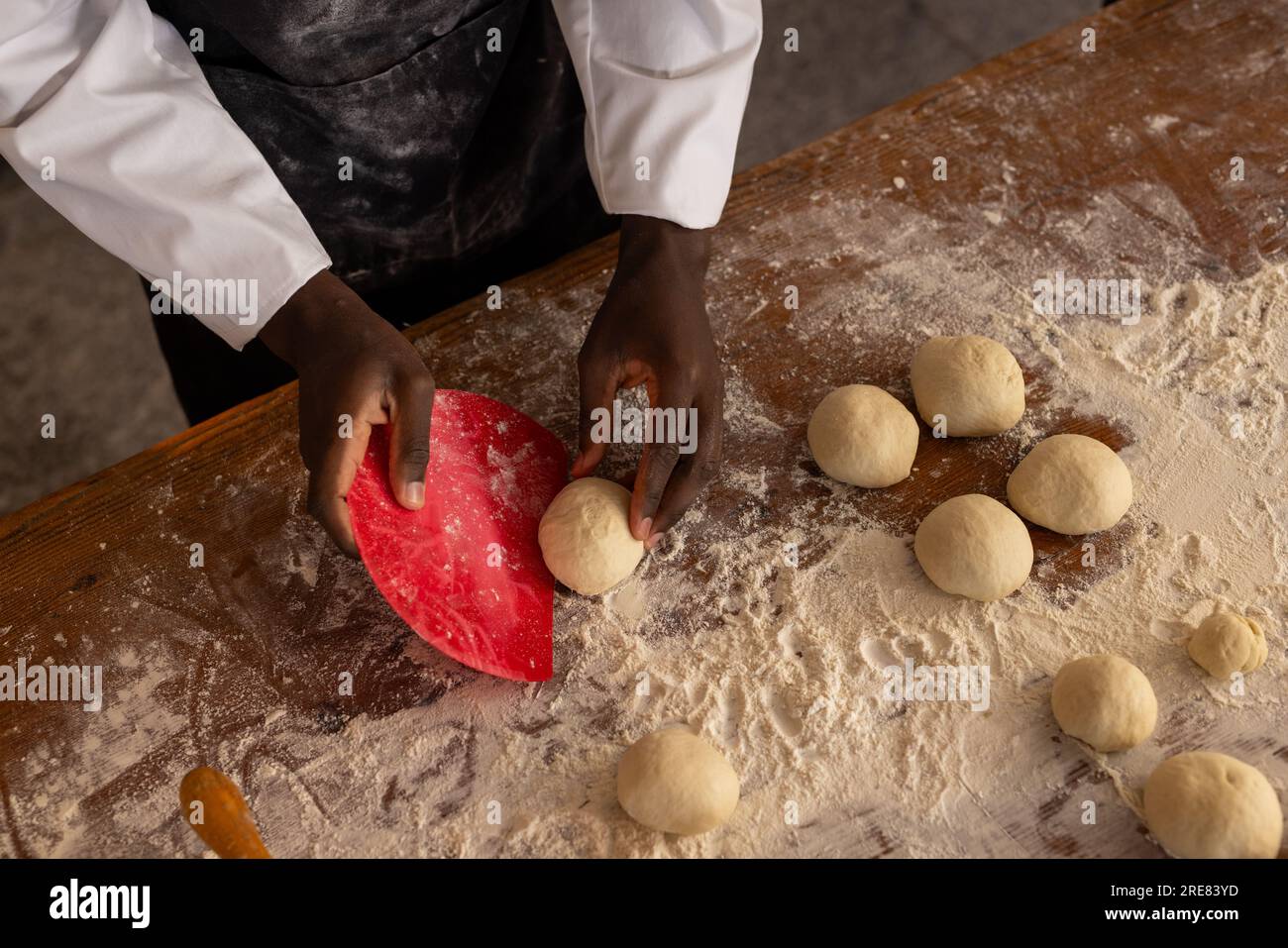 African american male baker in bakery kitchen forming dough for rolls ...
