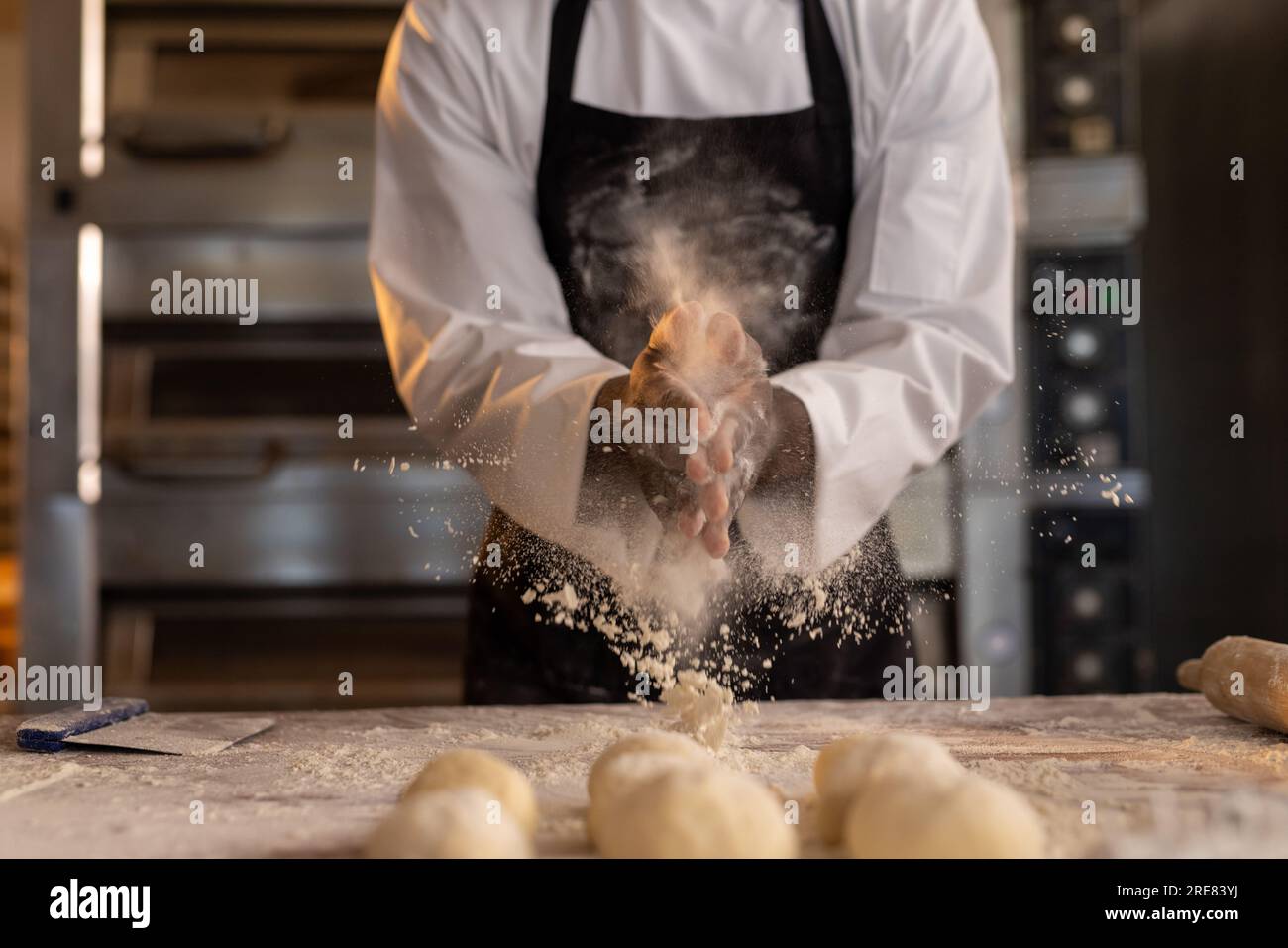 African american male baker in bakery kitchen clapping hands with flour ...