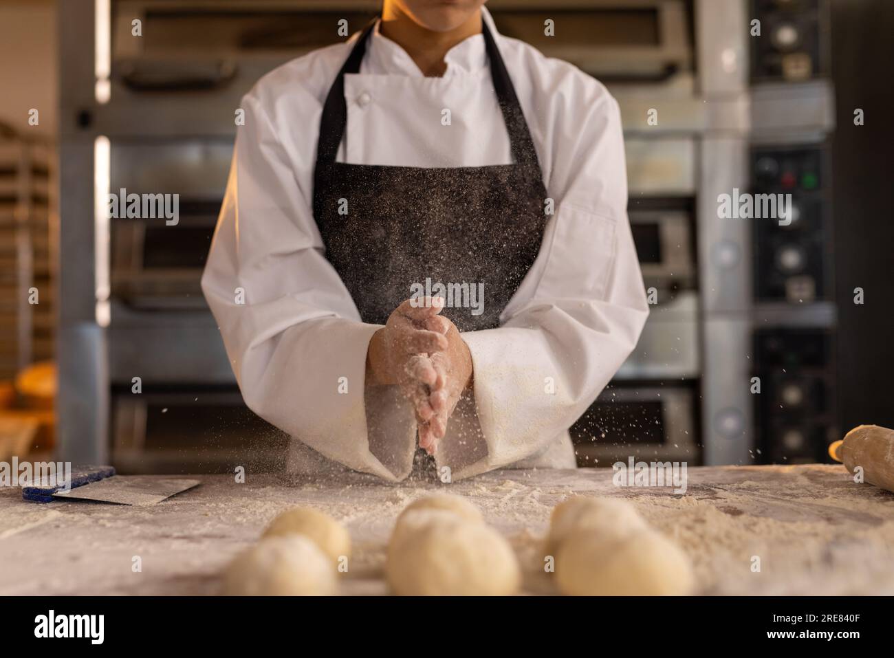 Asian female baker in bakery kitchen wearing apron and forming dough ...