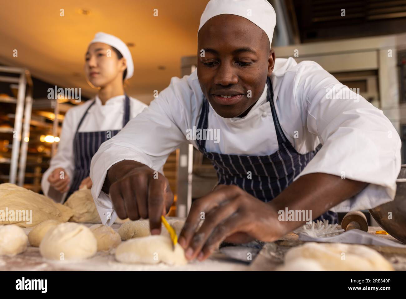 Happy diverse bakers wearing aprons in bakery kitchen and making rolls ...