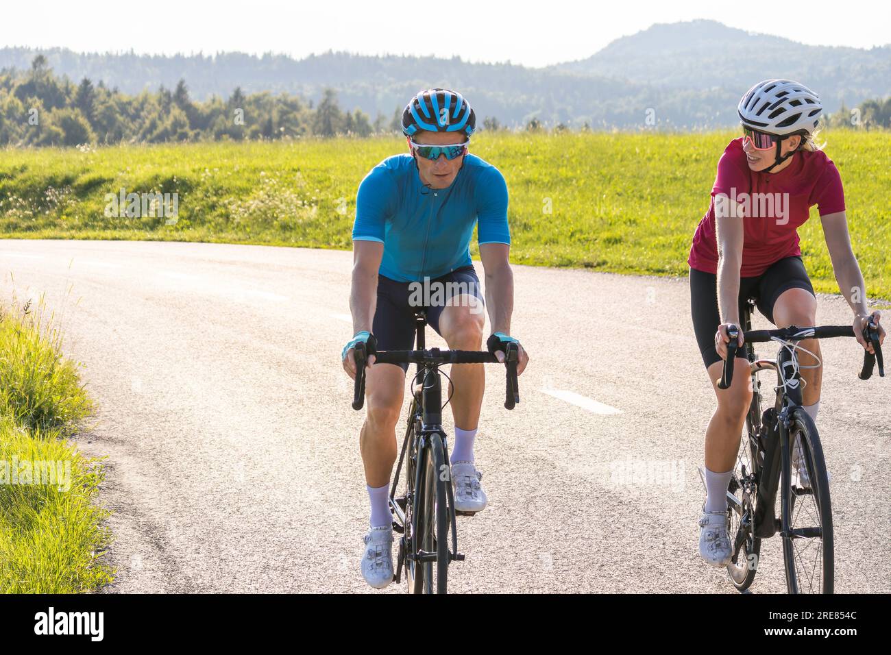 Cyclists couple on the road in summer cycling gear pedaling and gliding ...