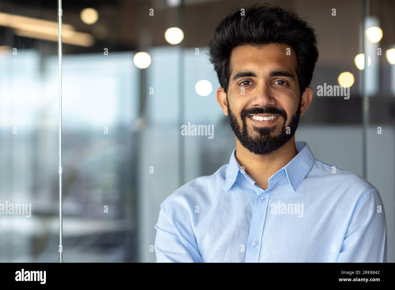 Portrait of a young Indian male student standing in an office, campus ...