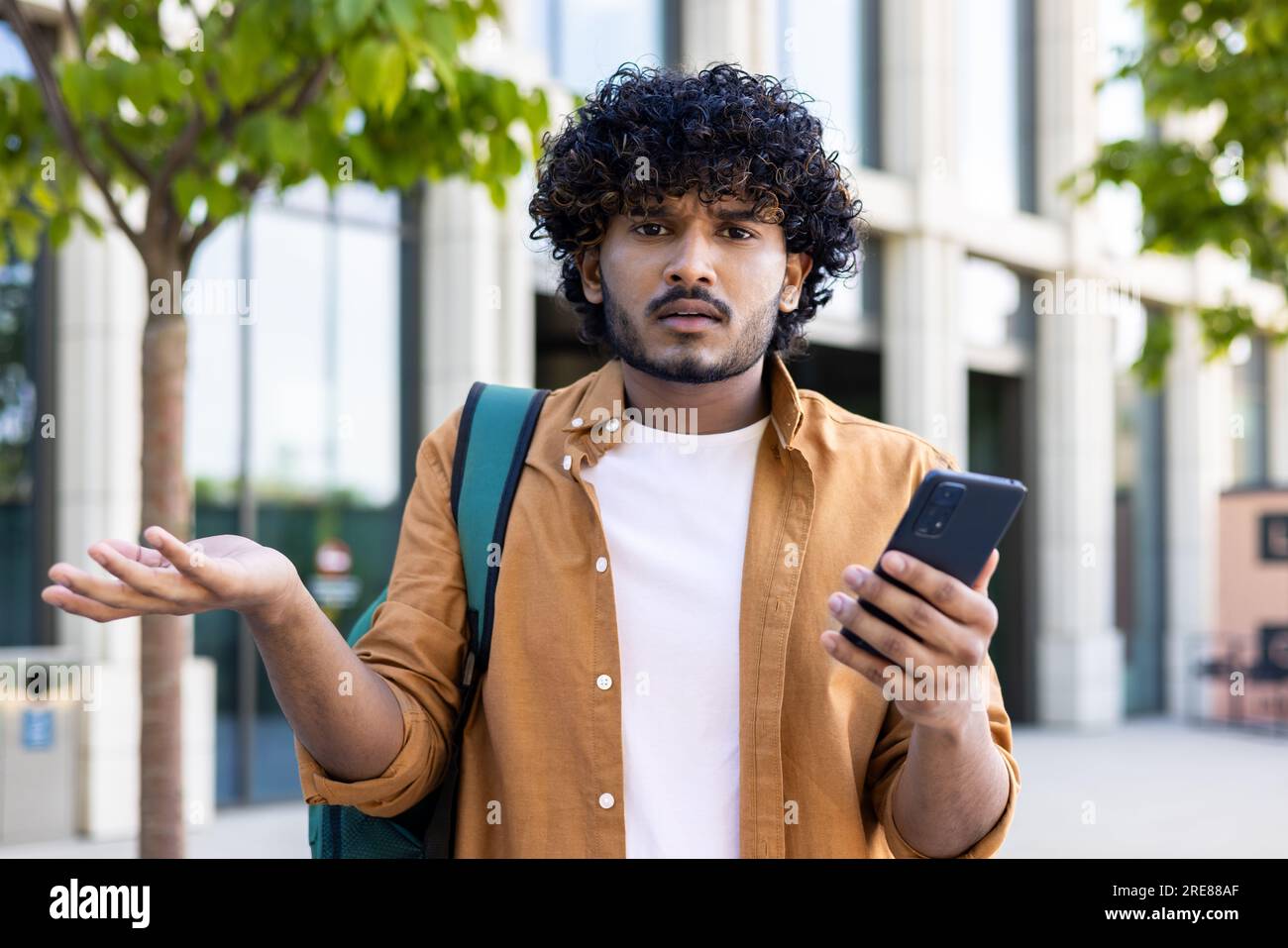 Worried young Indian man standing outside on the street, holding the ...
