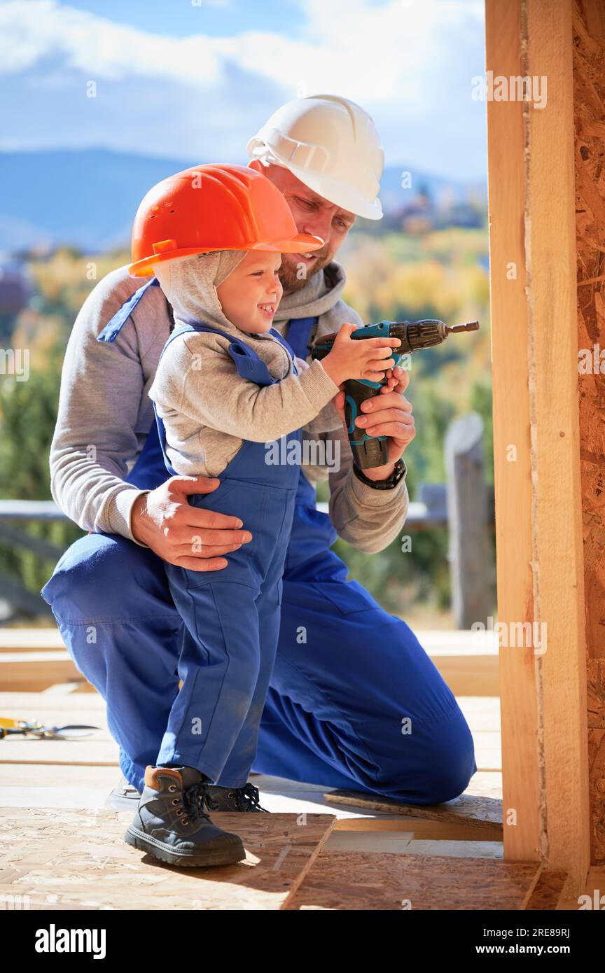 Father with toddler son building wooden frame house. Happy boy helping ...