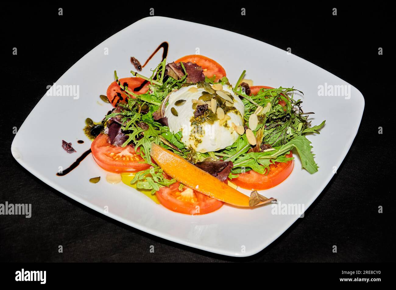 Burrata salad in white plate on black background Stock Photo - Alamy
