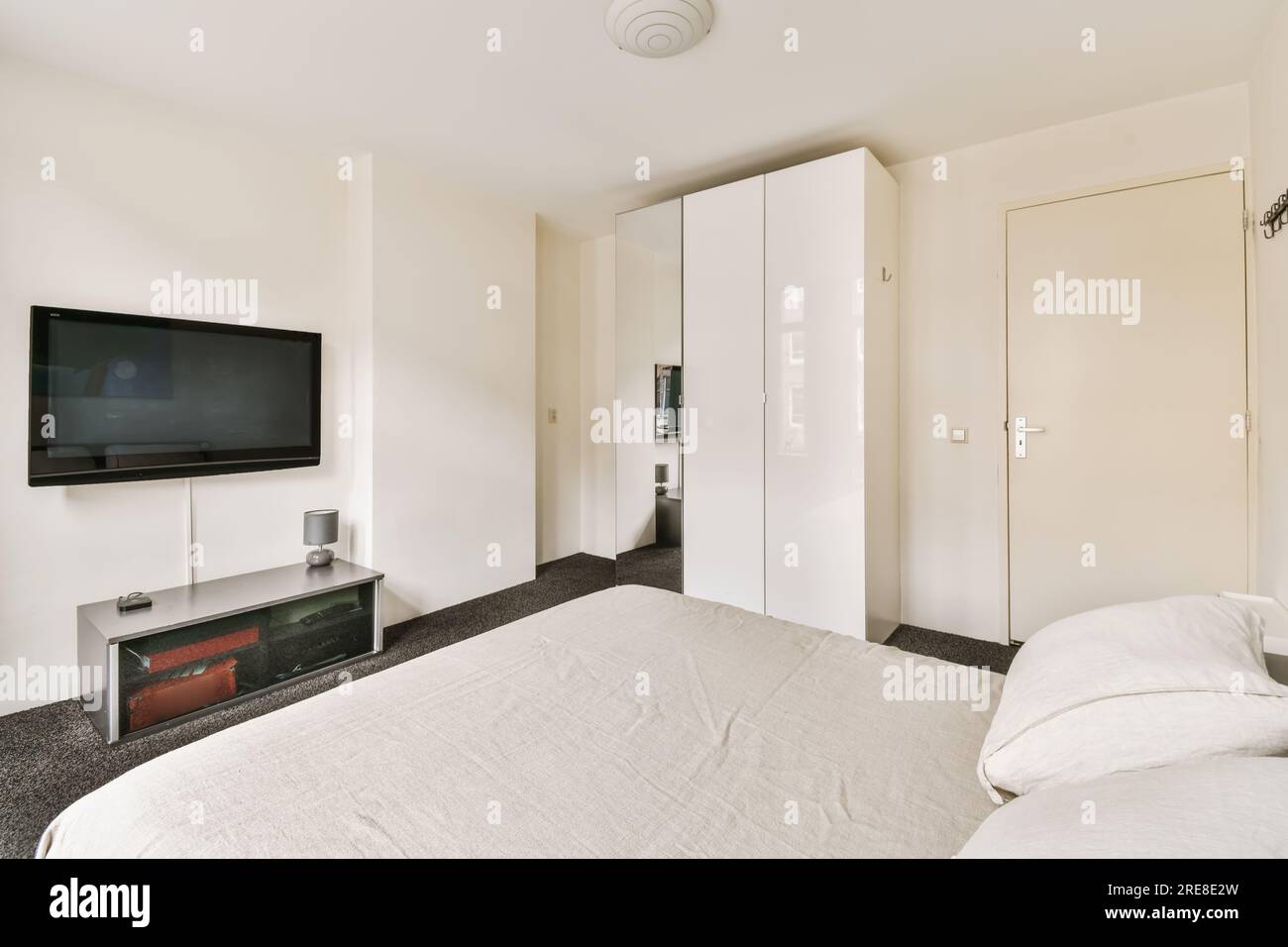 a bedroom with a flat screen tv on the wall and white bedding in front ...