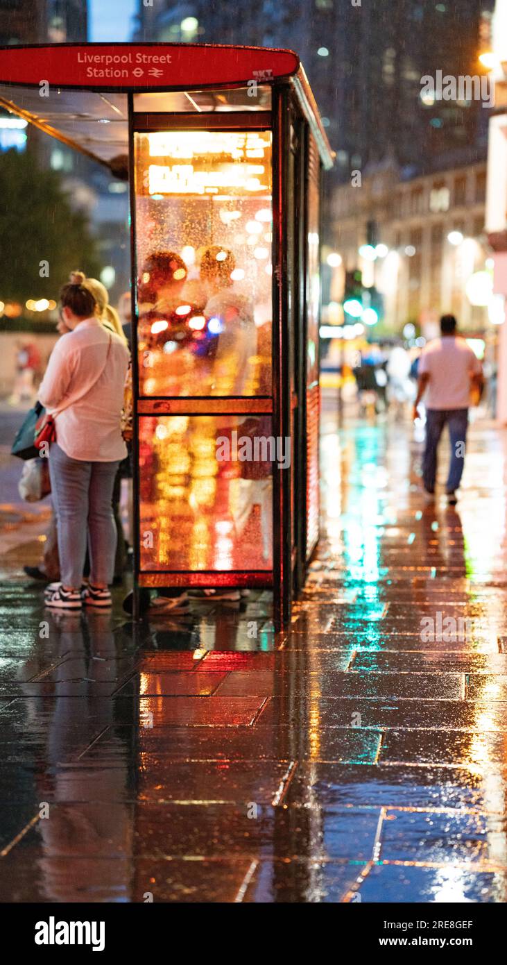 People sheltering from the rain at night on a London street under a bus ...