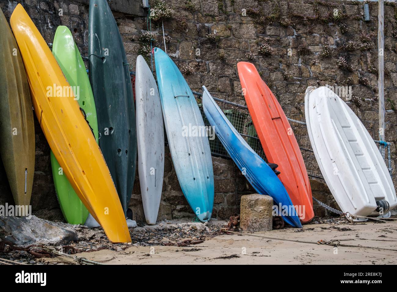 Colourful surfboards lean against stone wall at harbour, Cornwall ...