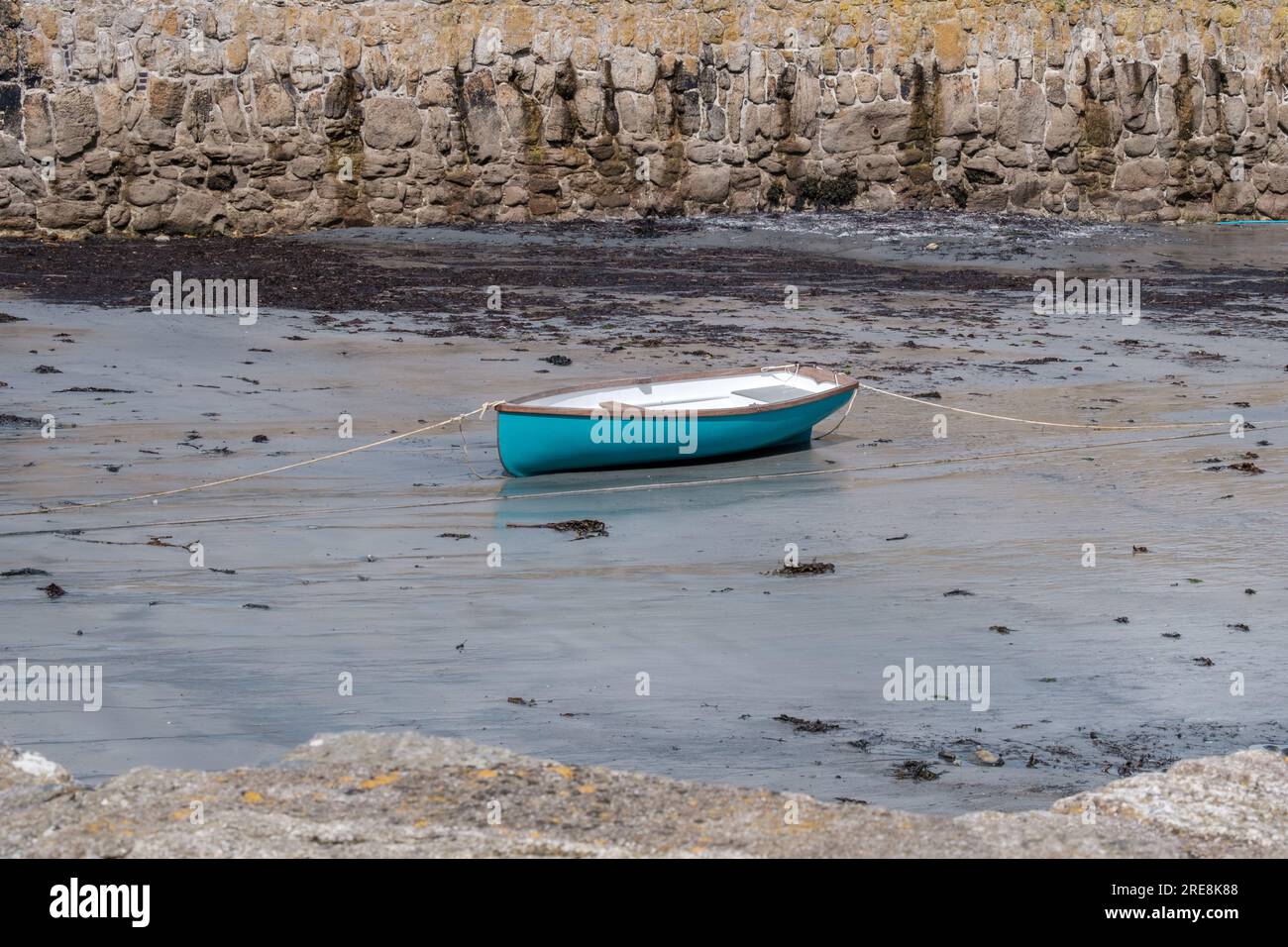A row boat sits beached at low tide with an ancient stone wall in the ...
