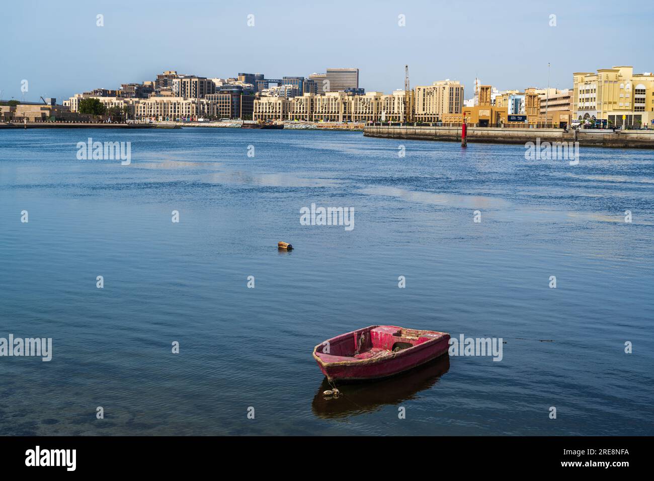 A photo of a red rowboat anchored in Dubai Creek with the city of Dubai ...