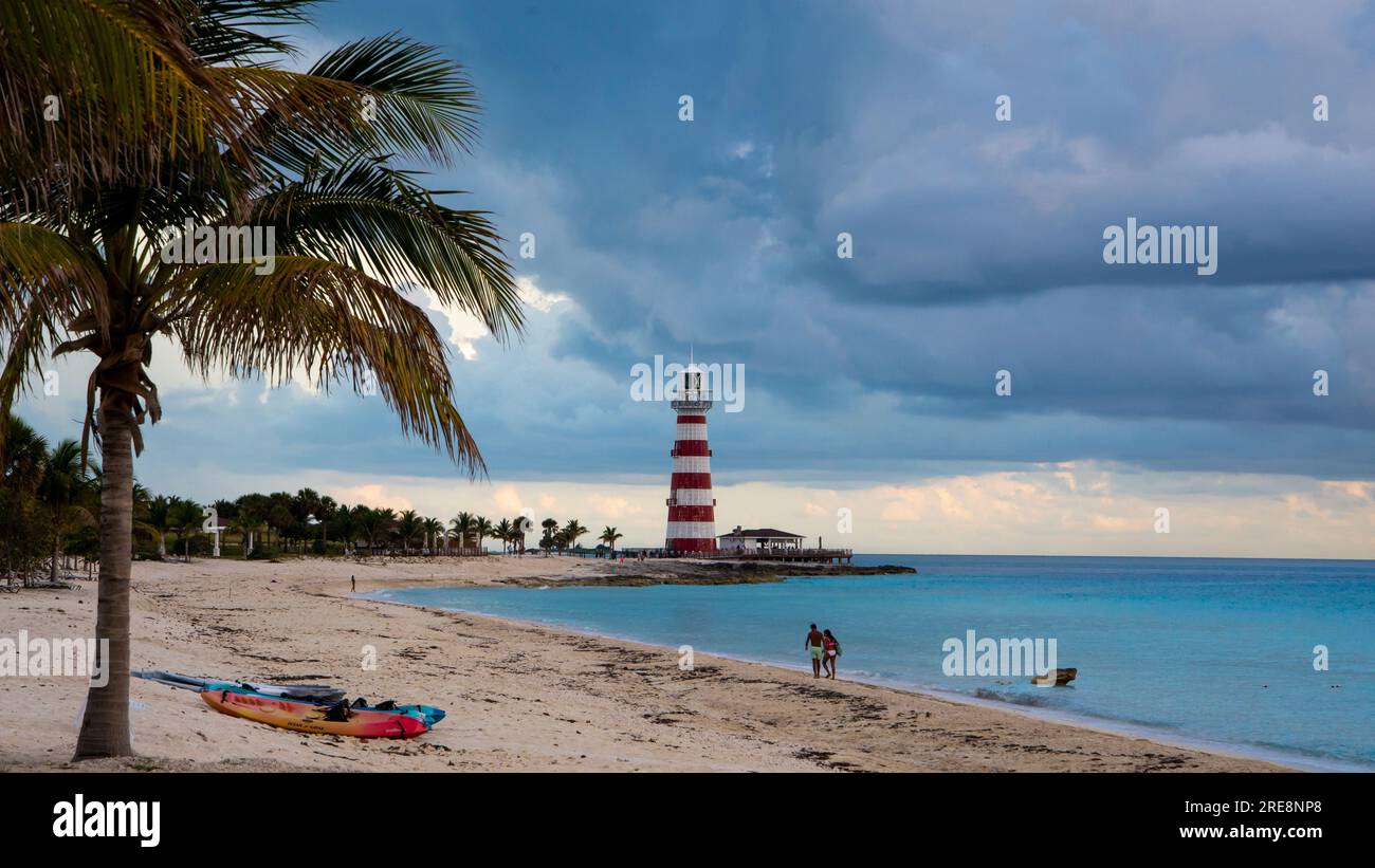At dusk two person walking along the beautiful beach with light tower ...