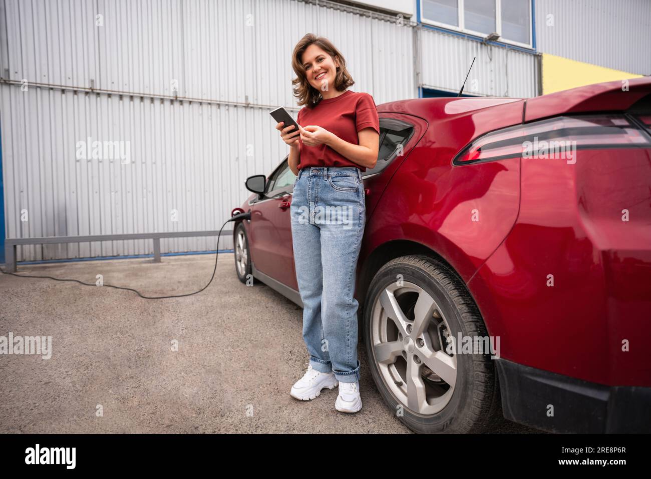 Woman with smartphone charging red electric car Stock Photo - Alamy
