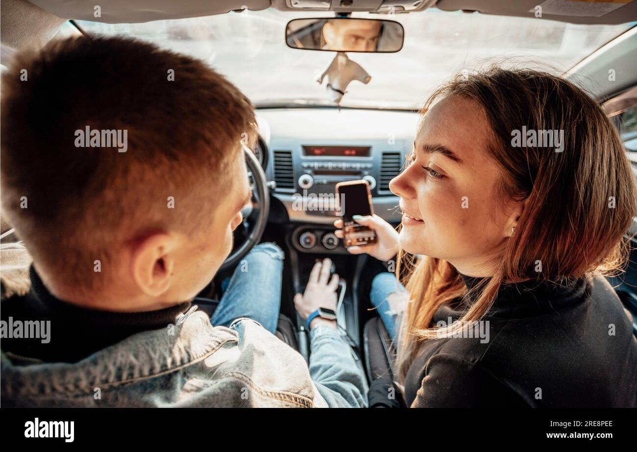 Young trendy couple discussing their route in the car with phones in ...