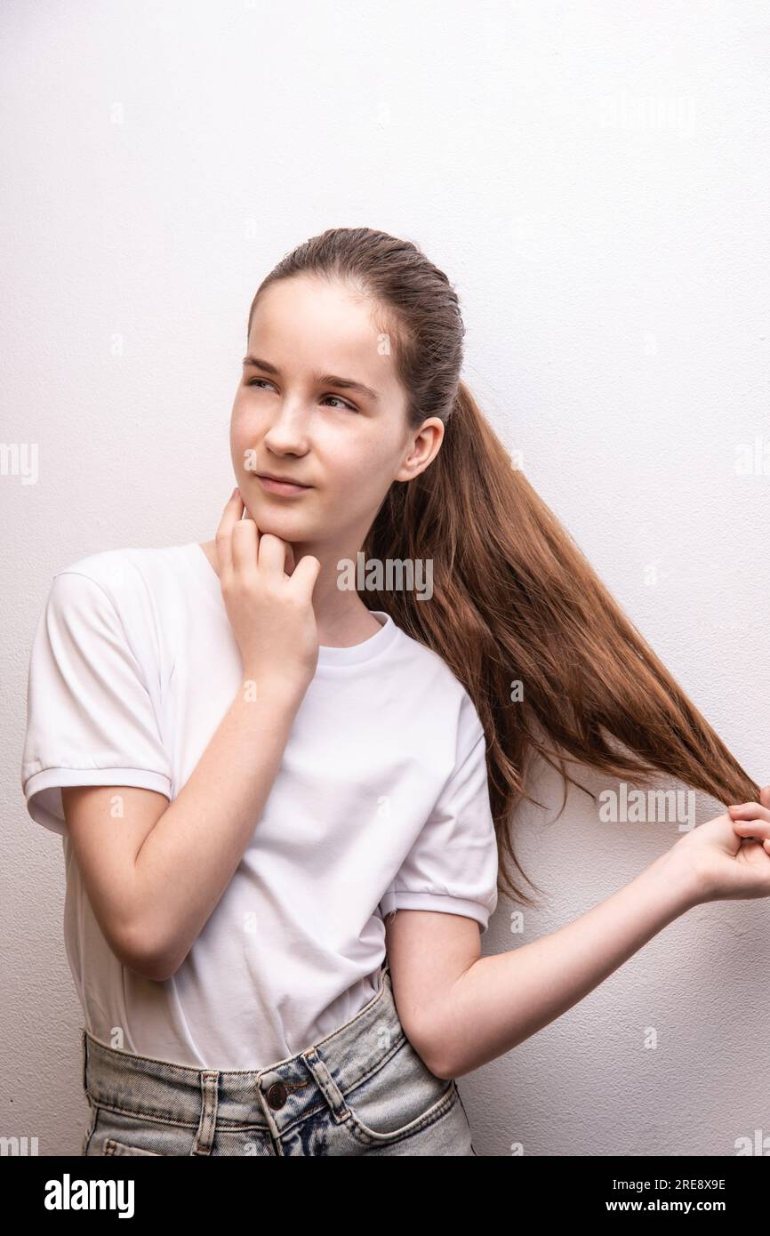 pensive girl touching thick healthy hair, look away, wearing white T ...