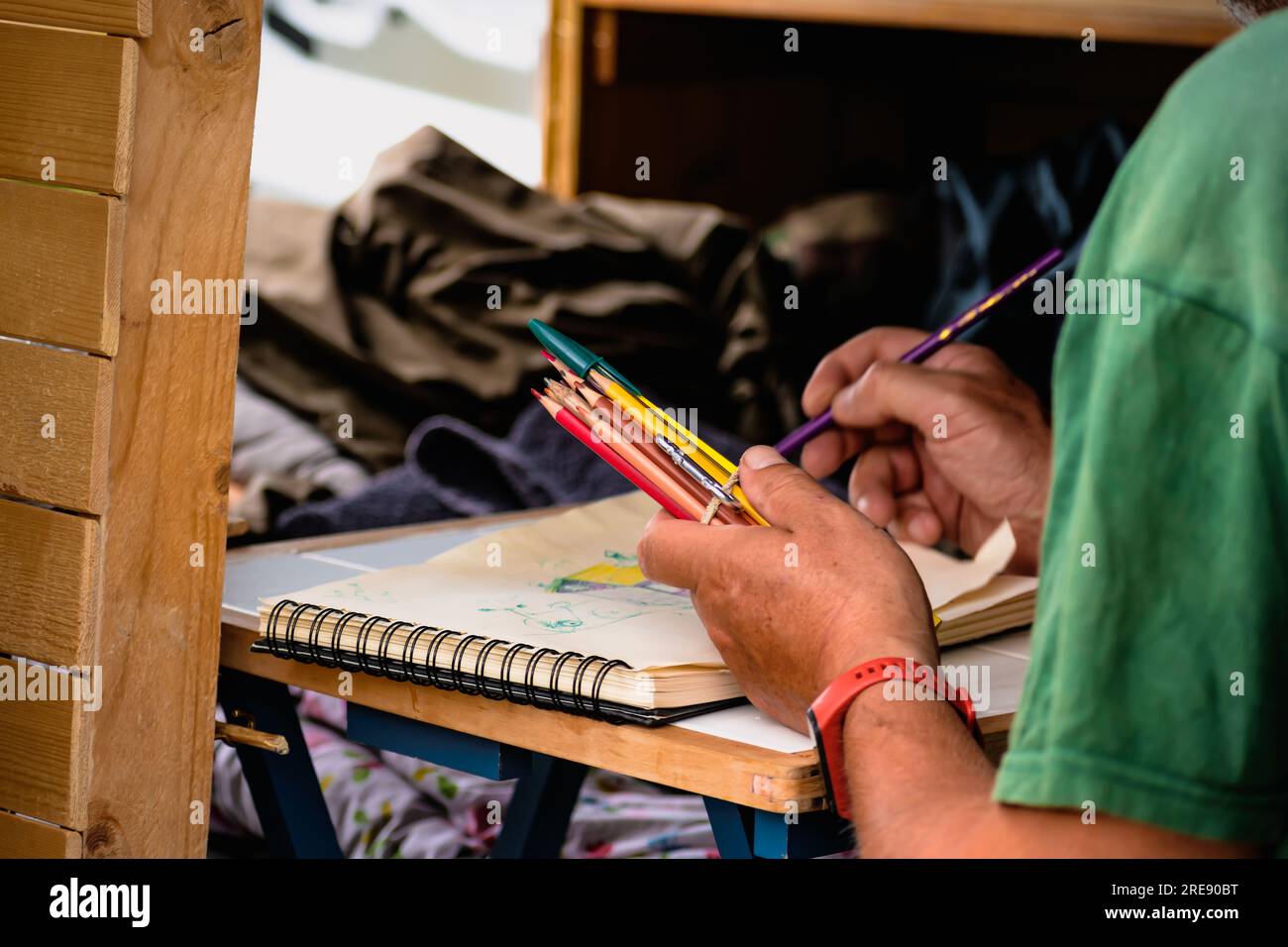 Man drawing on a notebook and holding pencils on a table in a converted ...