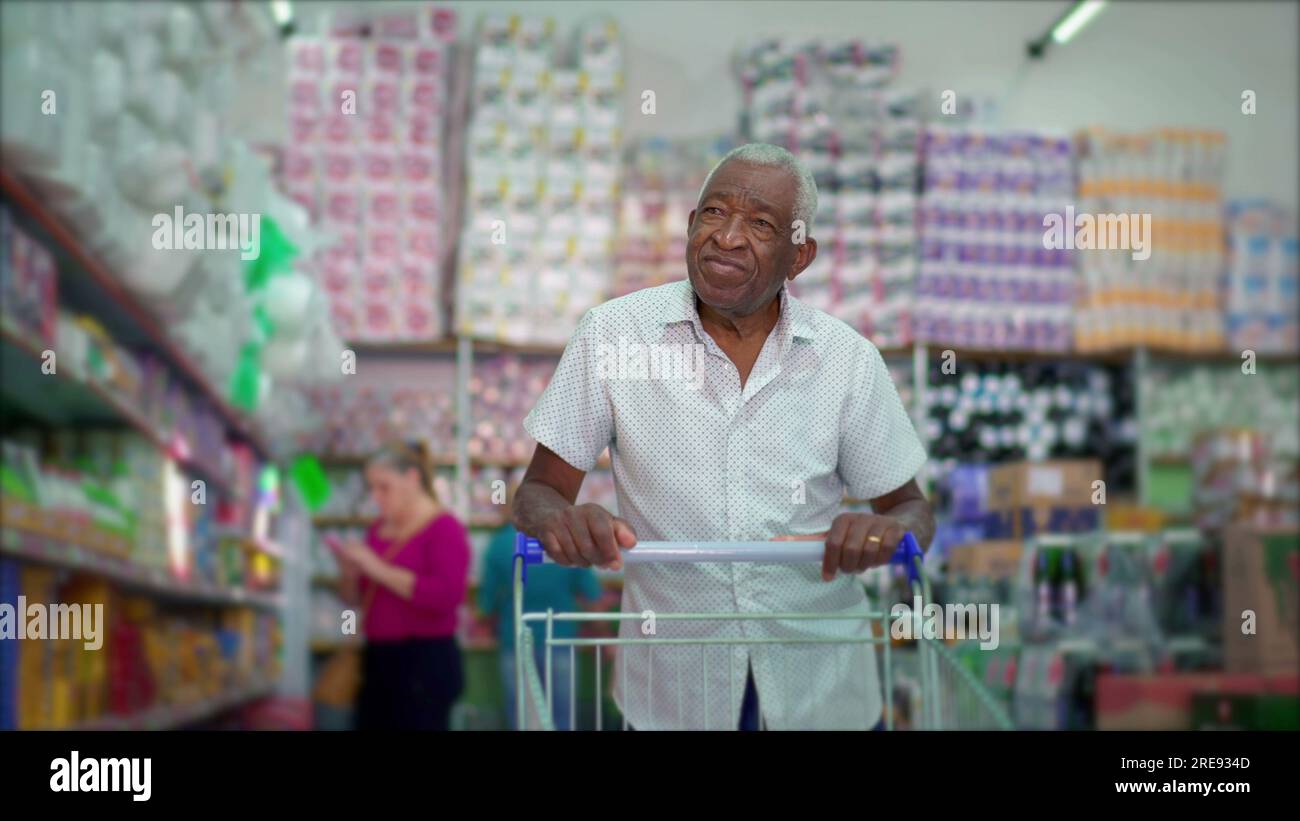 One senior black shopper pushing shopping cart at grocery store ...