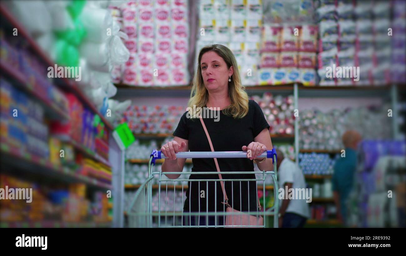 Female shopper walking at grocery store aisle pushing shopping cart ...