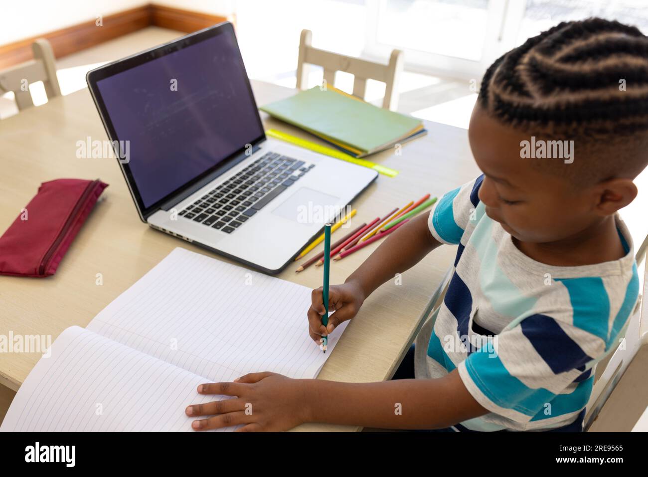 African american boy at desk in online class drawing and using laptop ...