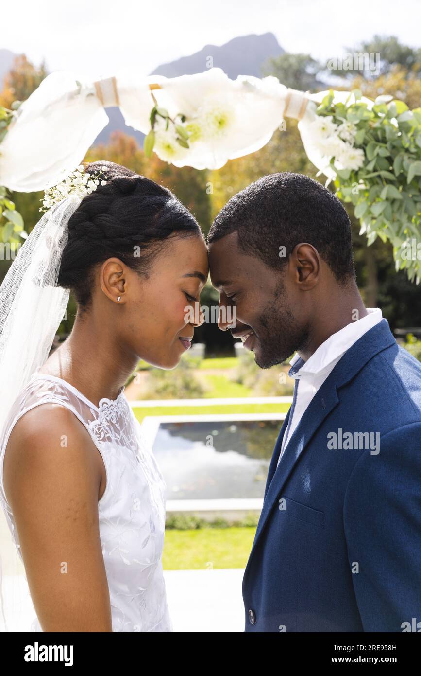 Happy african american bride and groom touching heads and smiling under ...