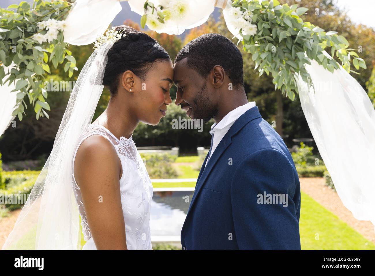 Happy african american bride and groom touching heads under wedding ...