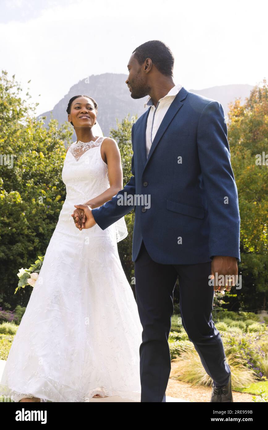 Happy african american bride and groom holding hands and walking in ...