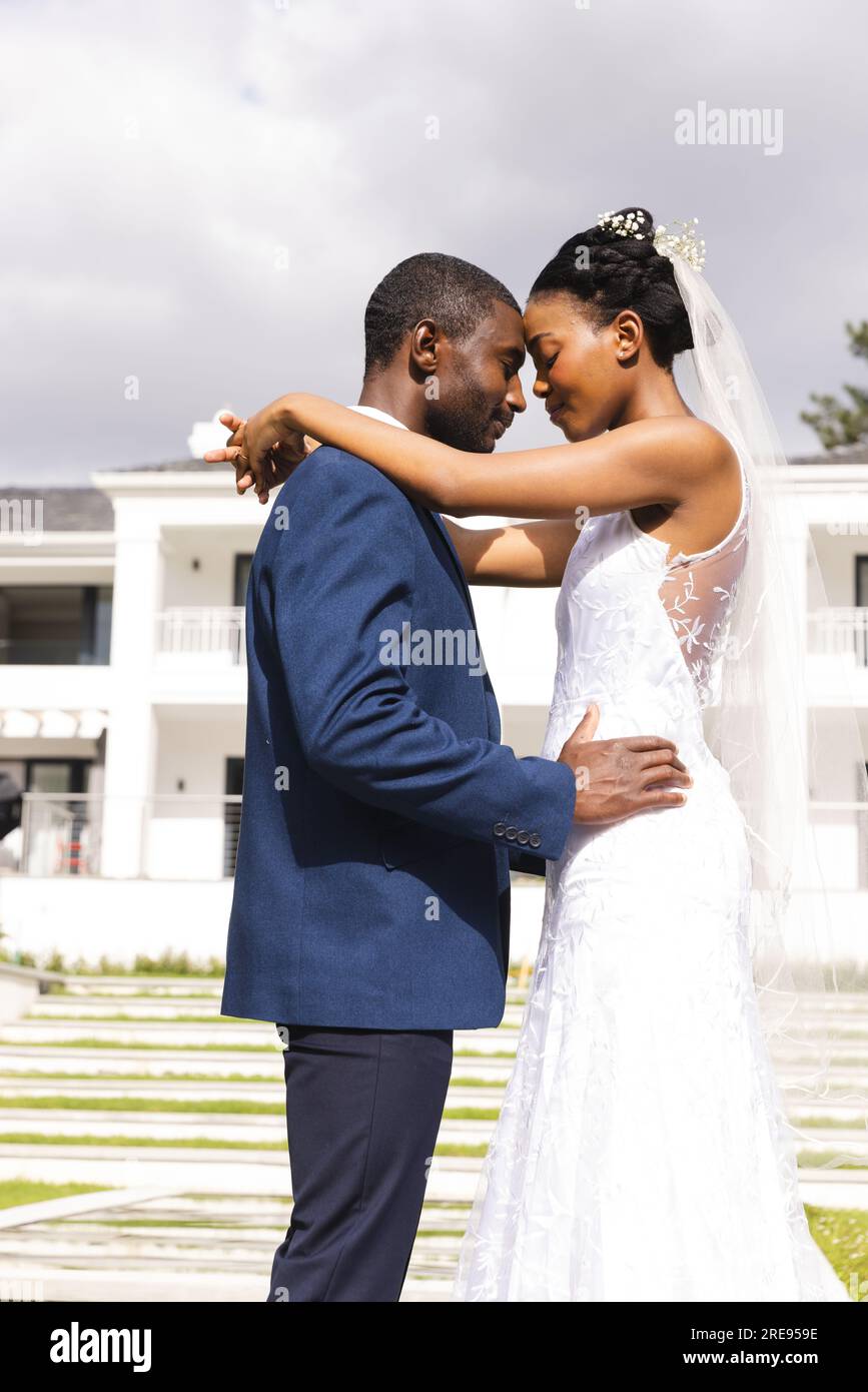 Happy african american bride and groom embracing in front of house in ...