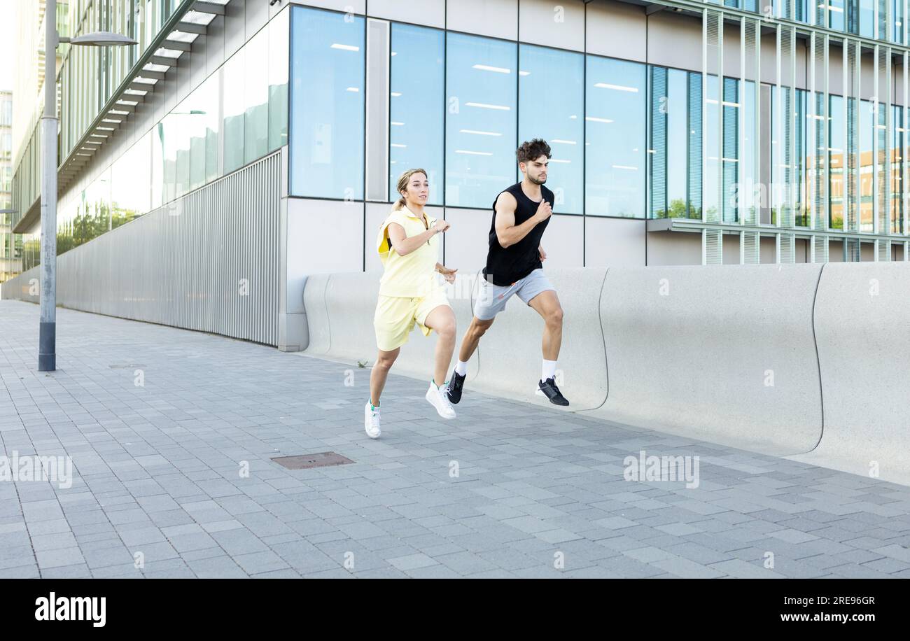 Focused athlete couple in sportswear and sneakers looking away while ...