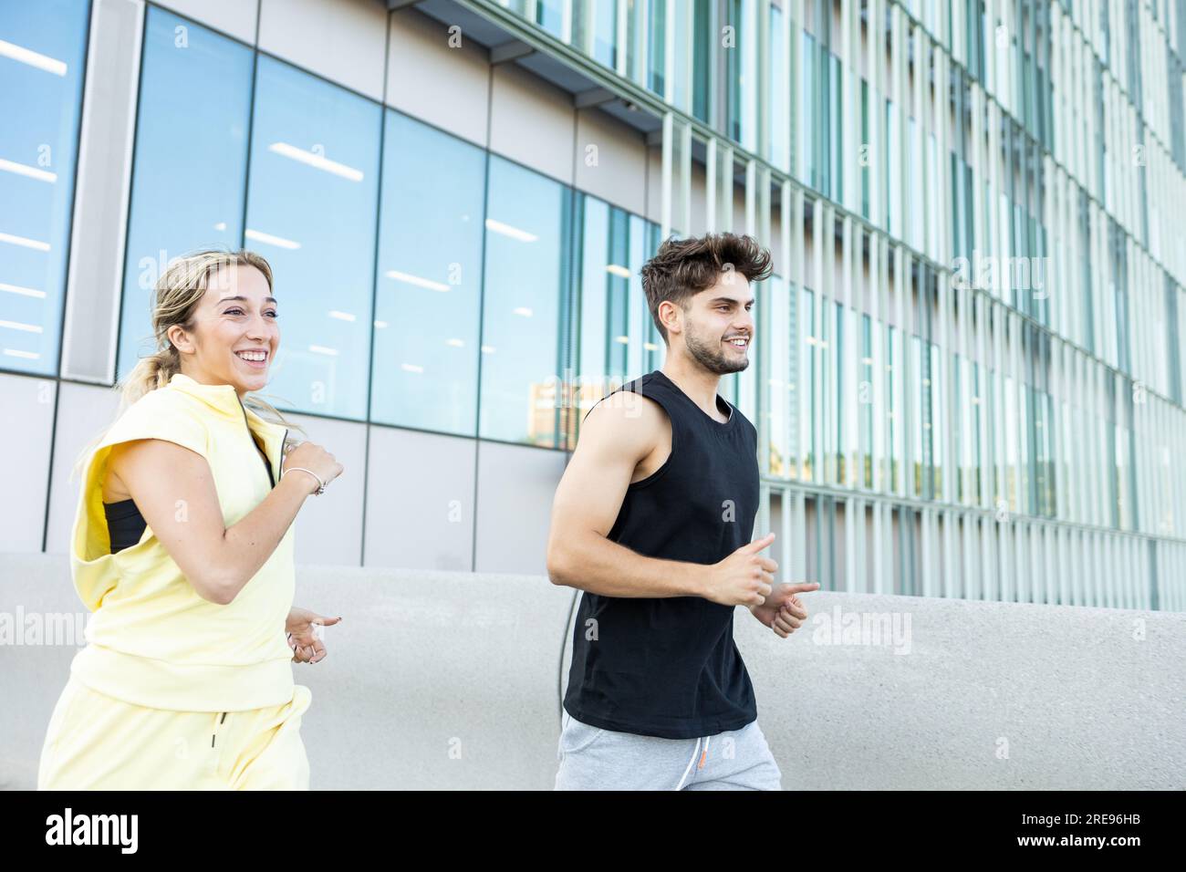 Focused happy athlete couple in sportswear while jogging on pavement ...