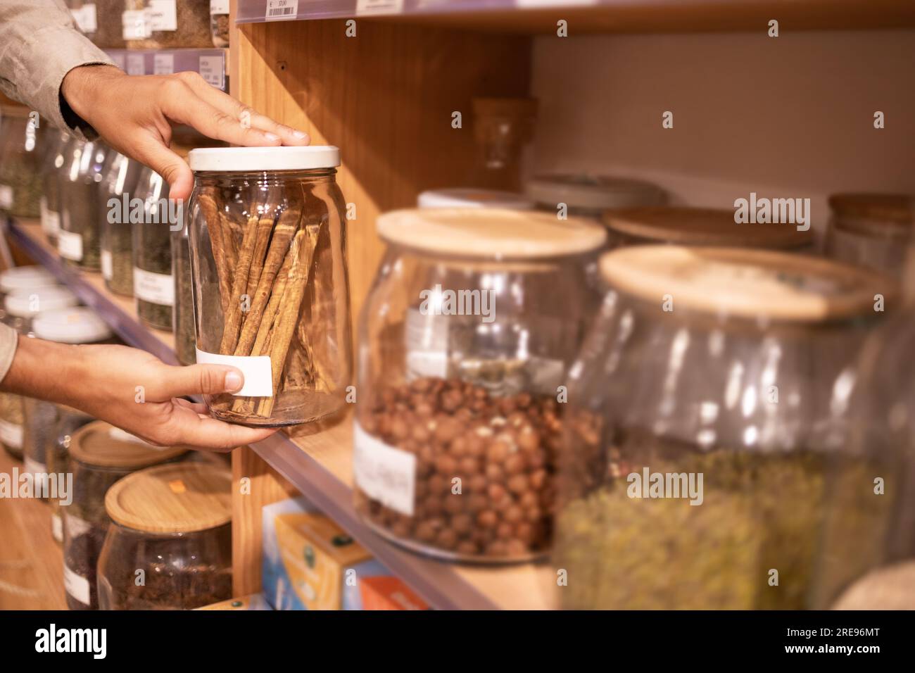 Crop unrecognizable male worker putting glass jar with cinnamon sticks ...