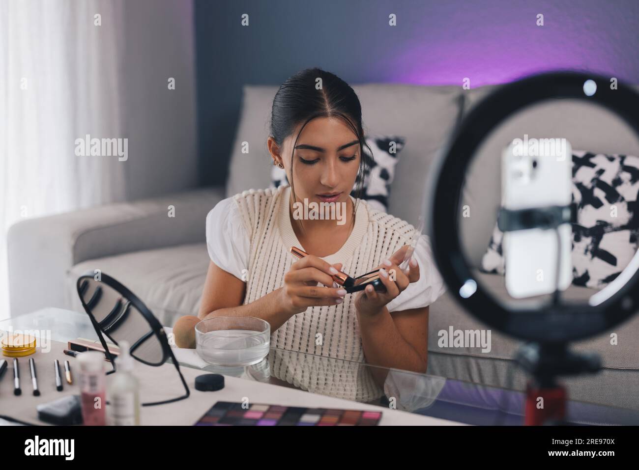 Young Hispanic female influencer applying bronzer with brush while ...