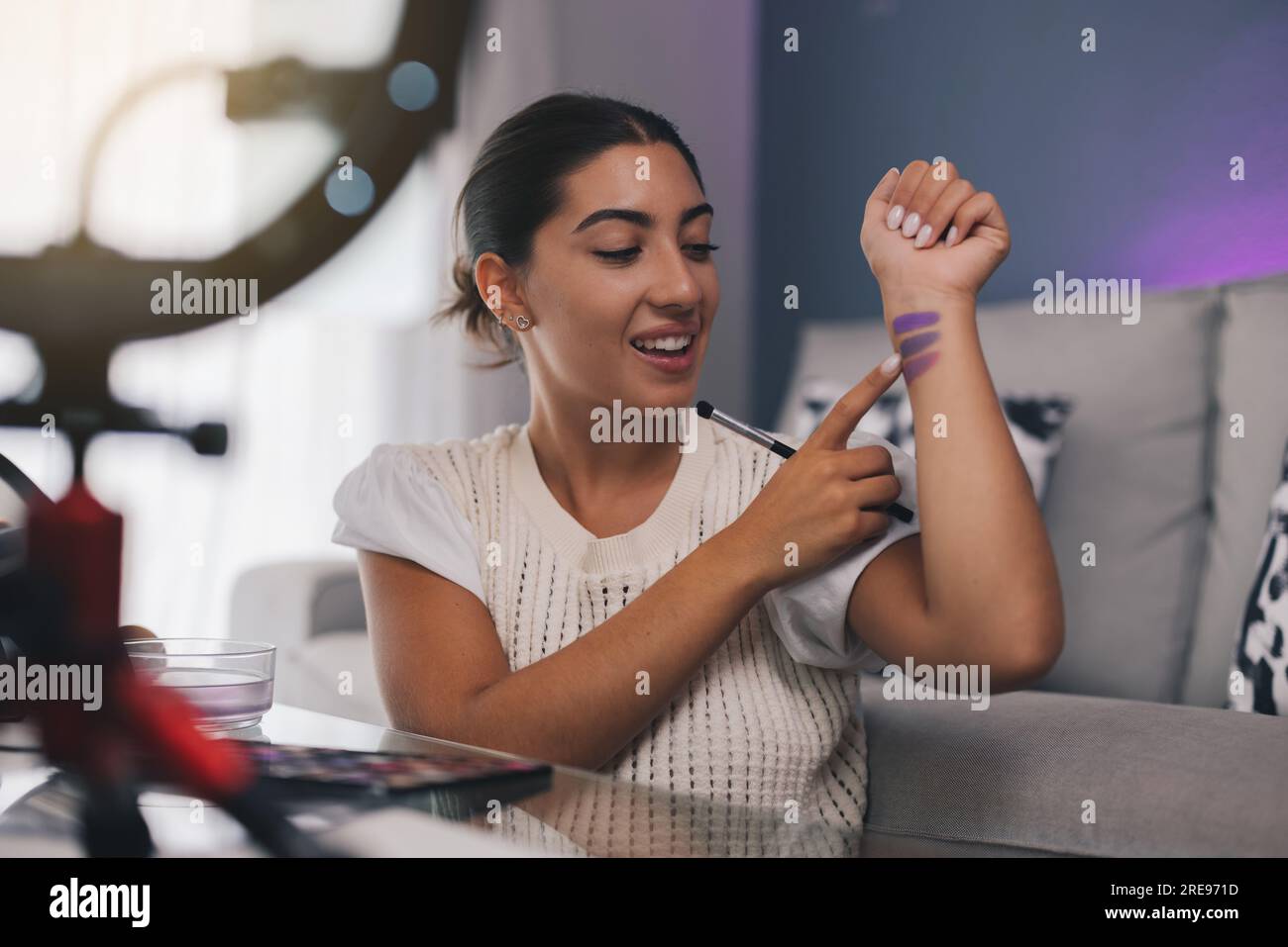 Smiling young Hispanic female influencer pointing at wrist with purple ...