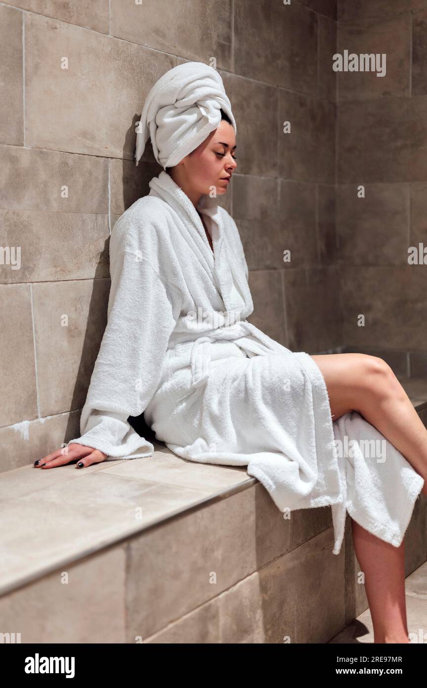 Side view of pensive young female in white bathrobe on head while ...