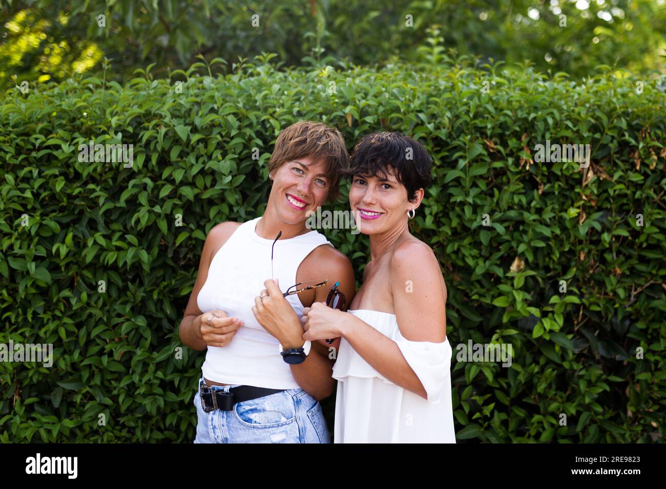 Adult friendly women sanding in green park while smiling sincerely ...