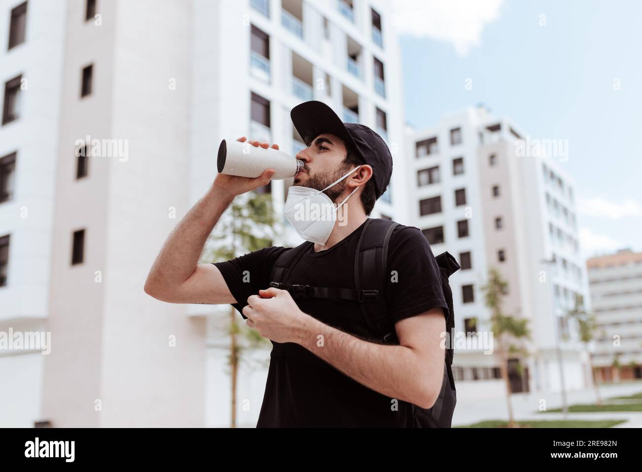 Low angle of male in respiratory mask and black wear drinking water ...