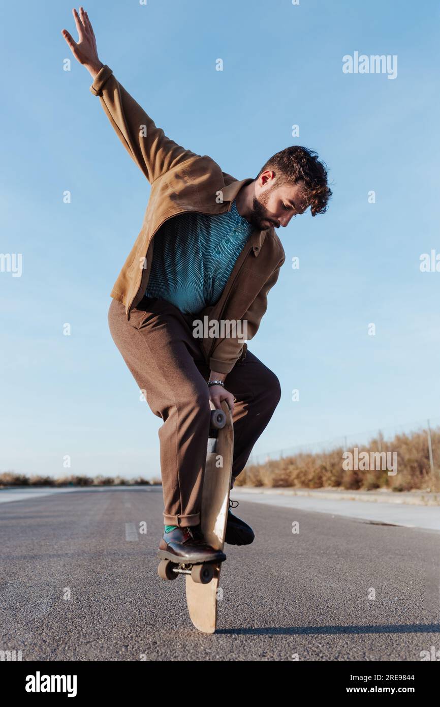 Full body young bearded male skater standing on edge of skateboard ...