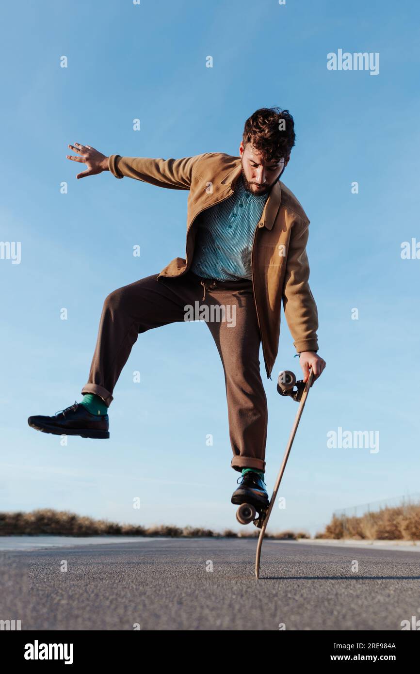Full body young bearded male skater standing on edge of skateboard ...