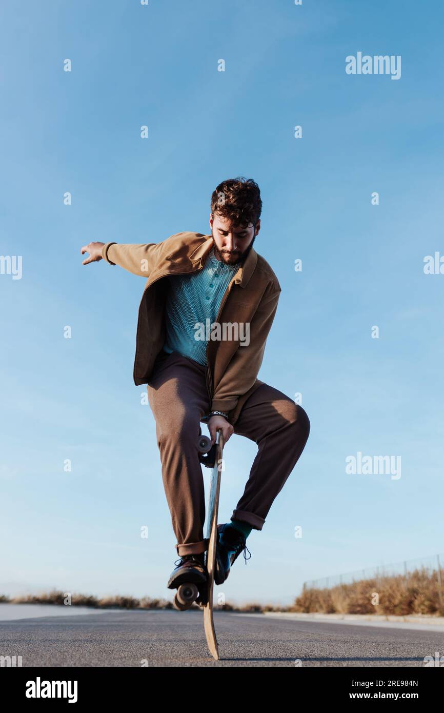 Full body young bearded male skater standing on edge of skateboard ...