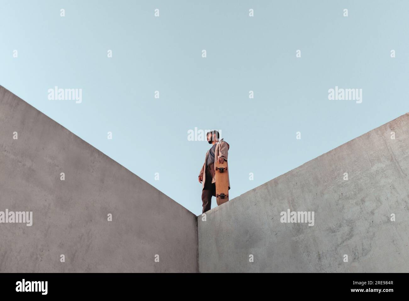 From below of young bearded male skater standing on high concrete ramp ...