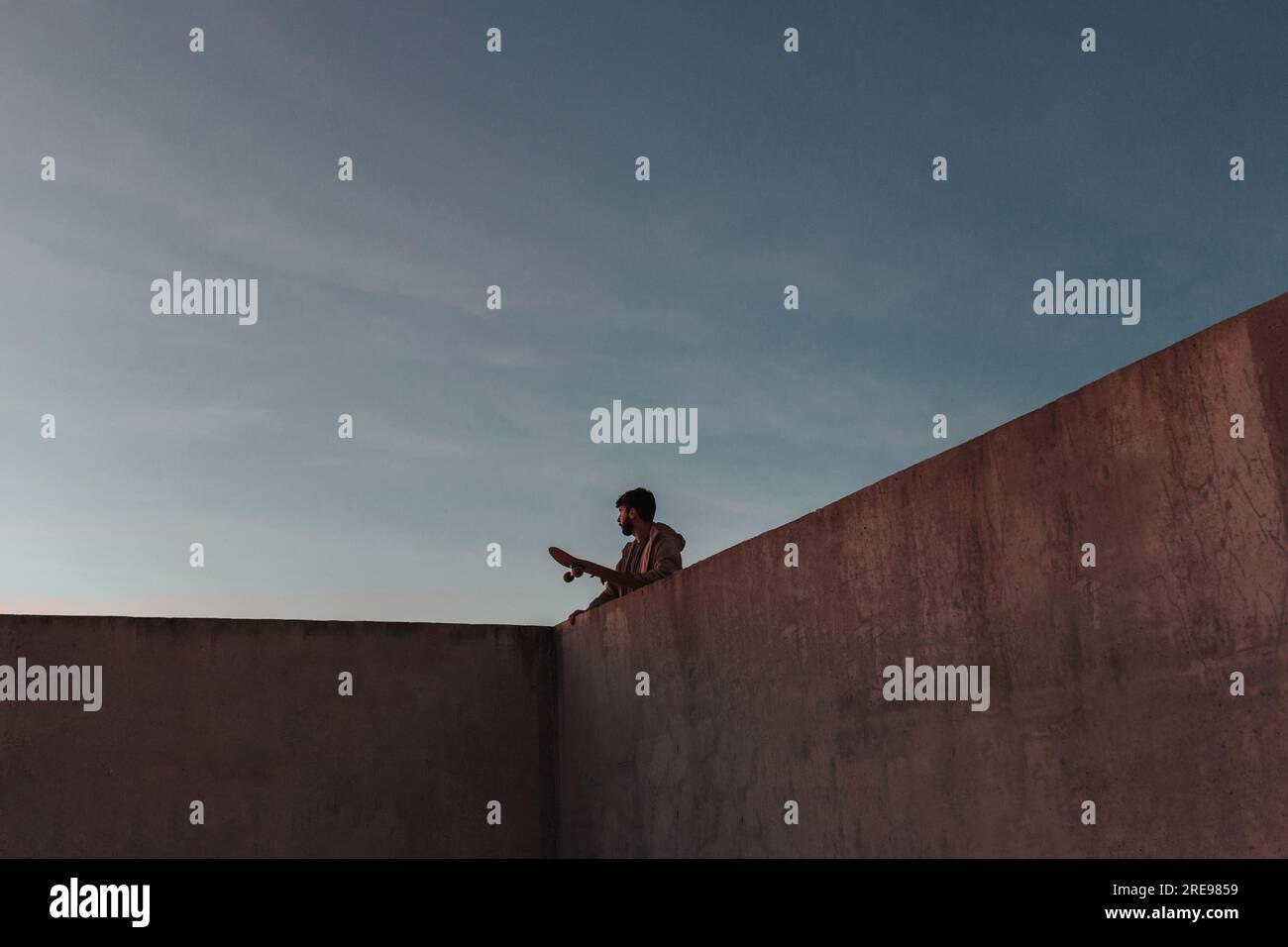 From below of young bearded male skater standing on high concrete ramp ...