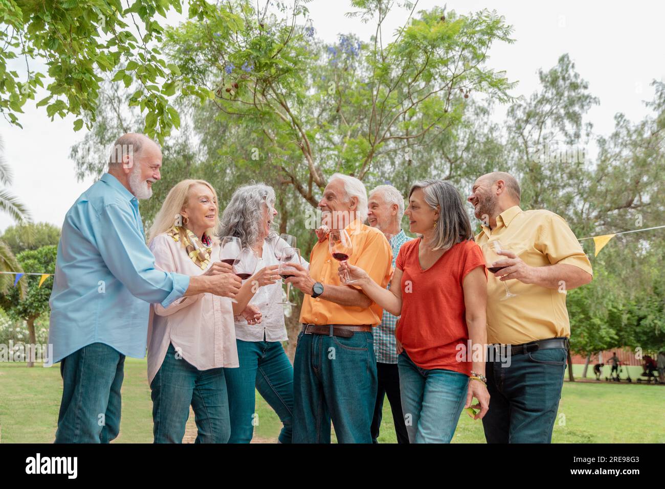 Group of happy middle aged friends standing in green park with glasses ...