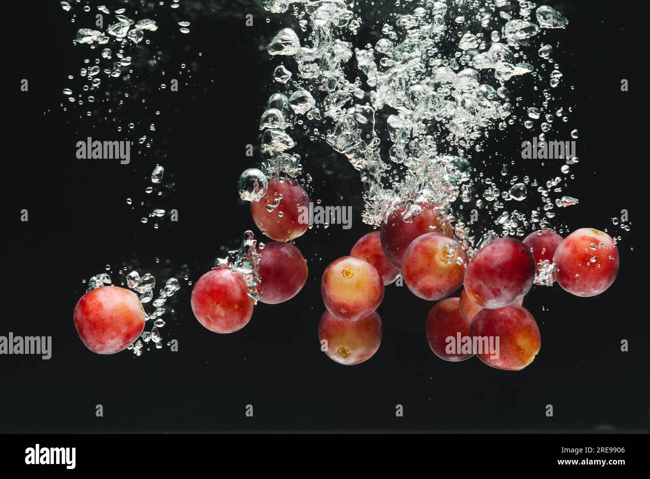 Close up of red grapes falling into water with copy space on black ...
