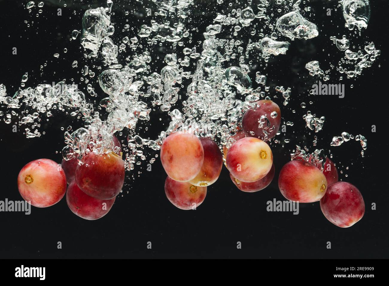 Close up of red grapes falling into water with copy space on black ...