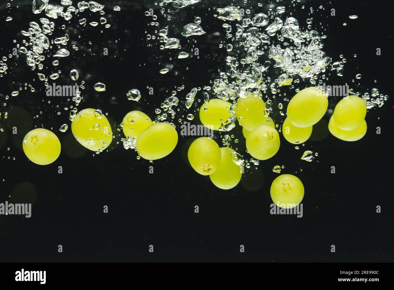 Close up of white grapes falling into water with copy space on black ...