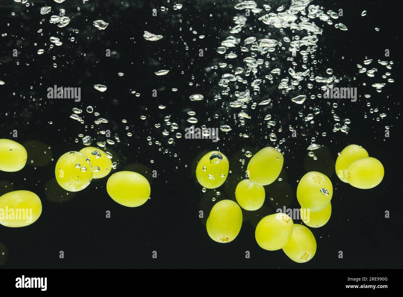Close up of white grapes falling into water with copy space on black ...