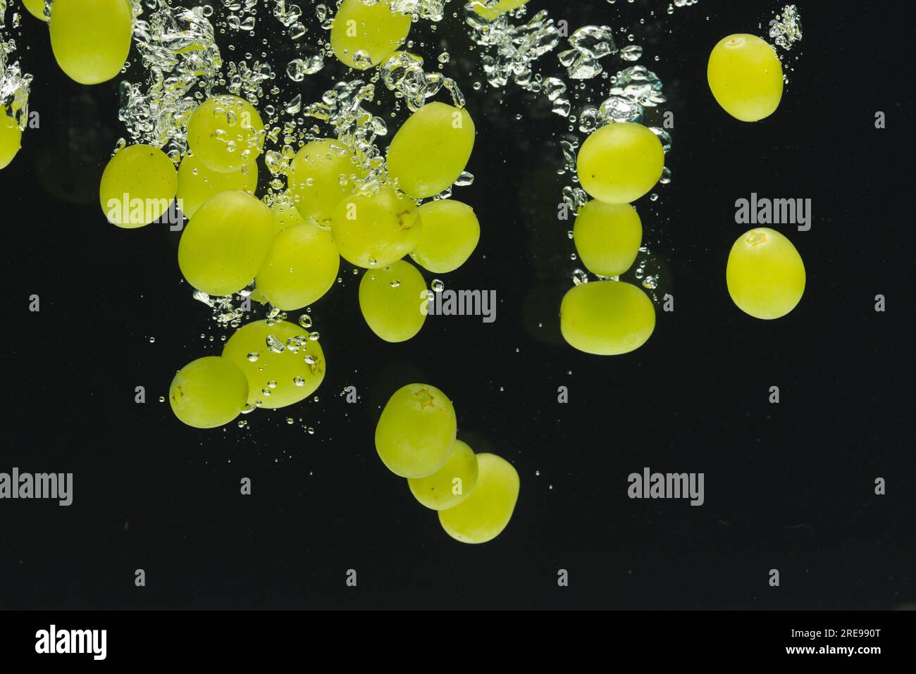 Close up of white grapes falling into water with copy space on black ...