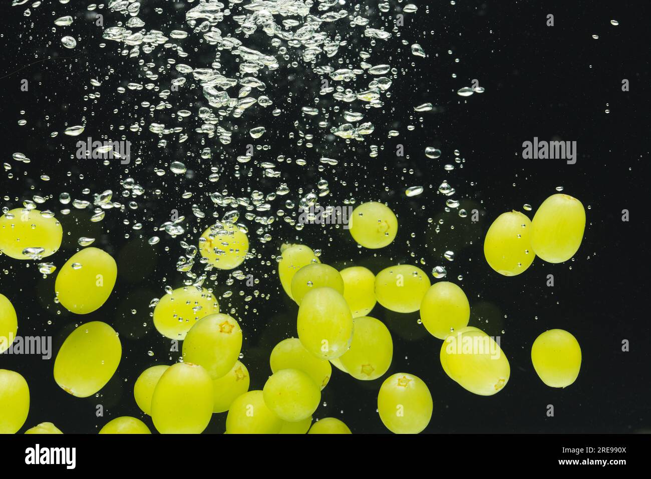 Close up of white grapes falling into water with copy space on black ...