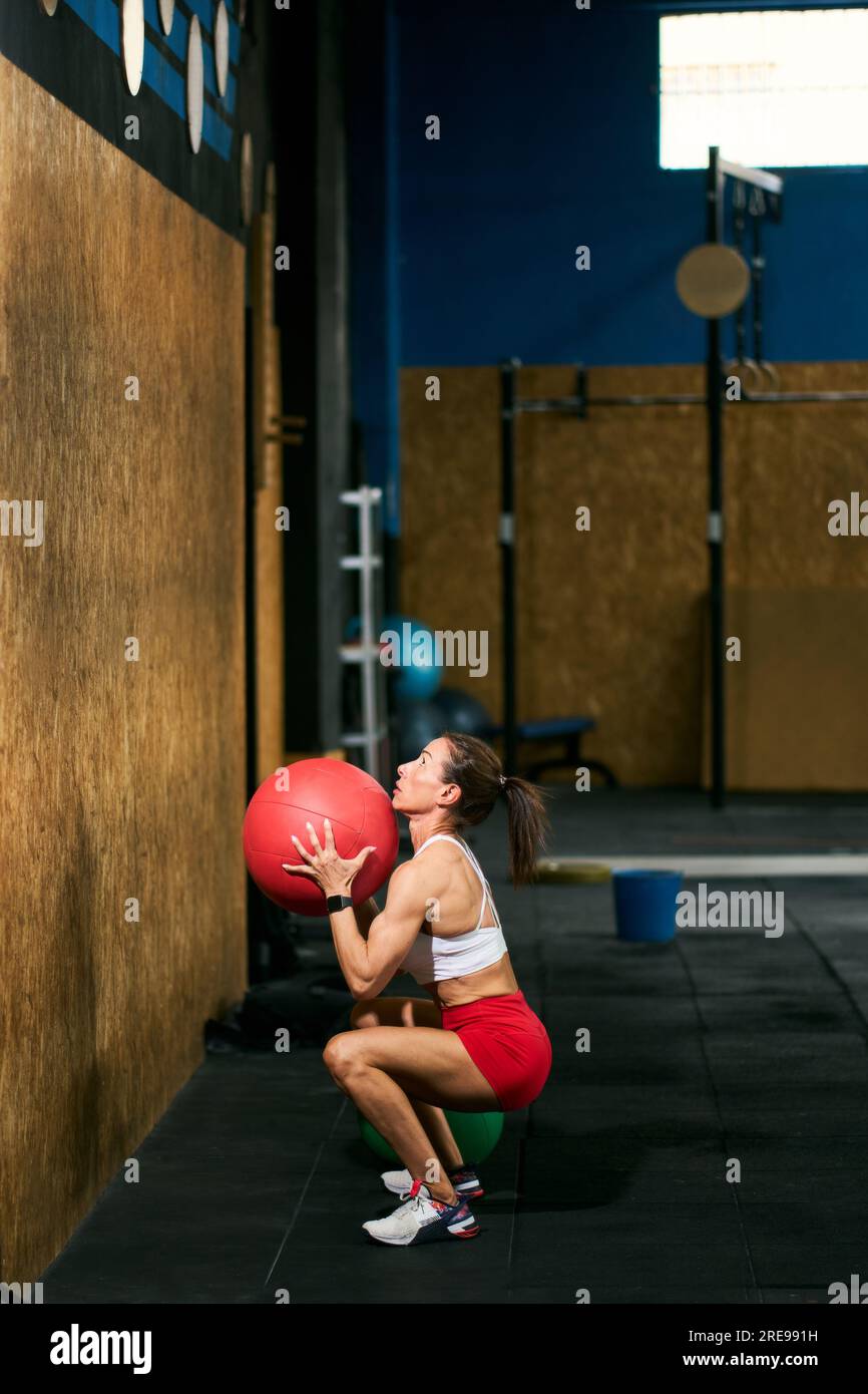 Full body side view of sportive female athlete crouching and throwing ...