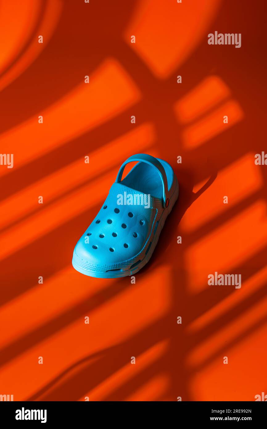 From above of plastic blue clog with holes placed on orange floor ...