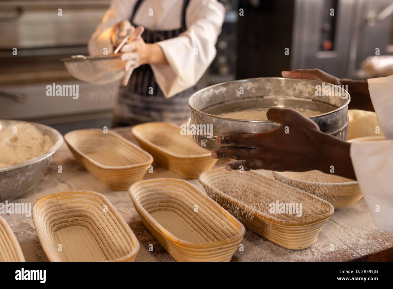 Diverse bakers wearing aprons in bakery kitchen and pouring flour on ...